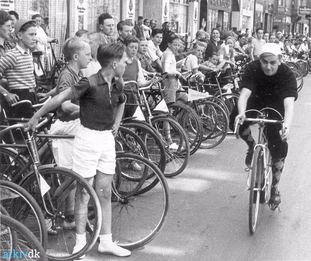 arkiv.dk | Cykelløb, unge tilskuere og rytter Langs husfacaderne står ...