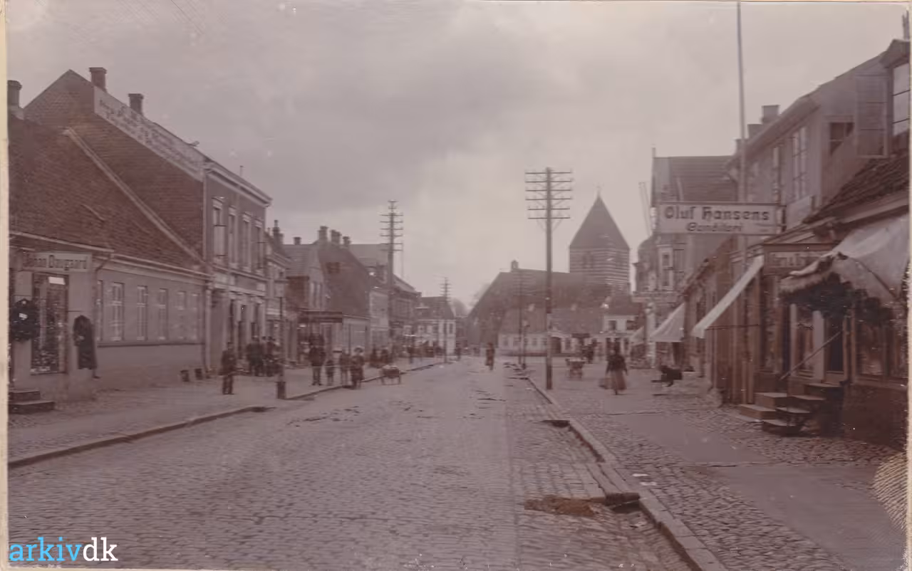 arkiv.dk | Folkeliv på Storegade i Stege med Conditori Oluf Hansen til højre og tøjforretning ...