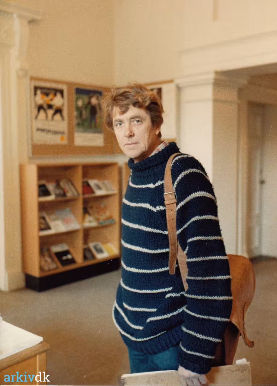 arkiv.dk | Maleren Jeppe Andreas Larsen står i et bibliotekslokale iført stribet sweater.